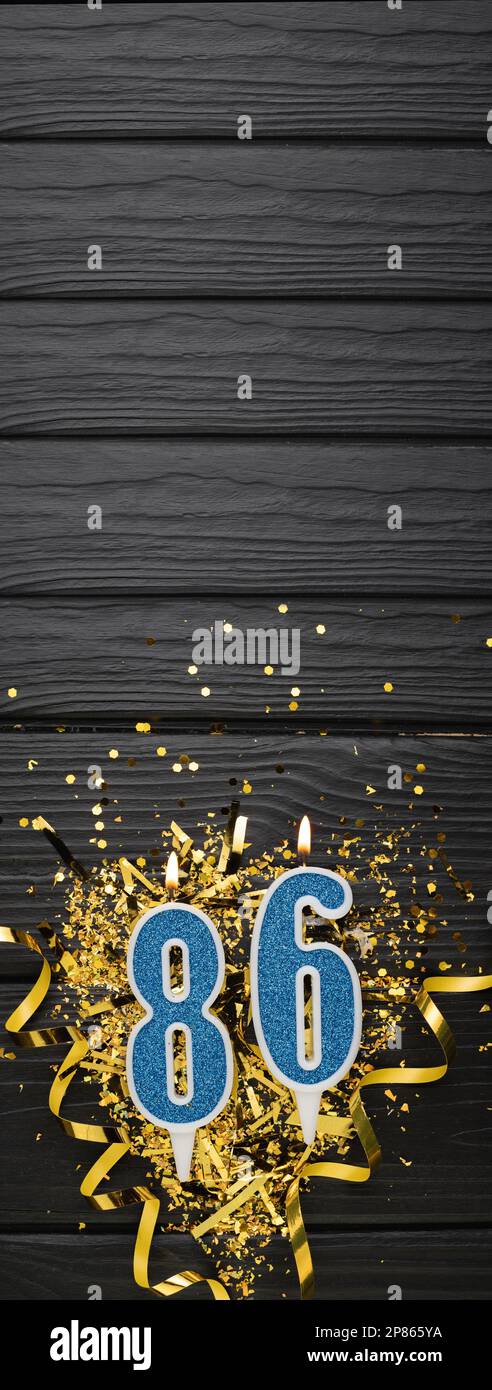 Number 86 blue celebration candle and gold confetti on dark wooden ...