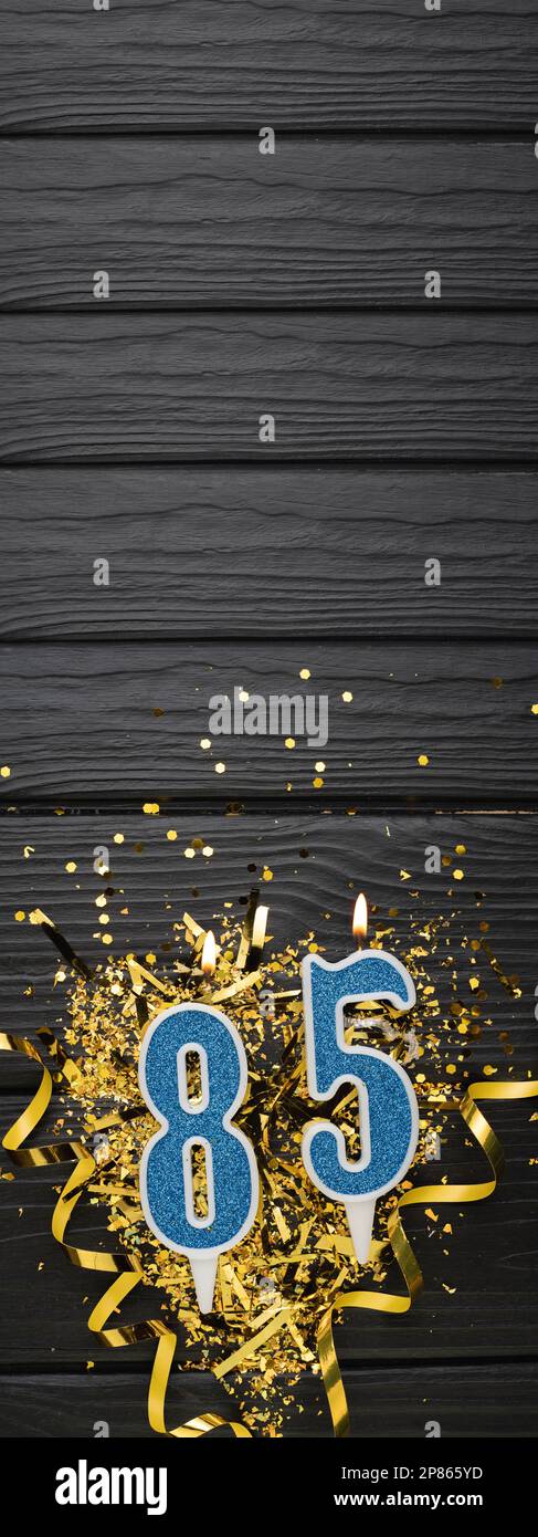 Number 85 blue celebration candle and gold confetti on dark wooden ...