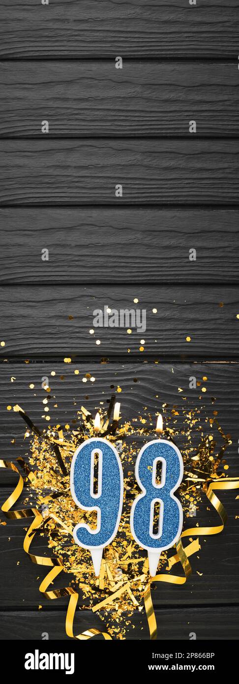 Number 98 blue celebration candle and gold confetti on dark wooden ...