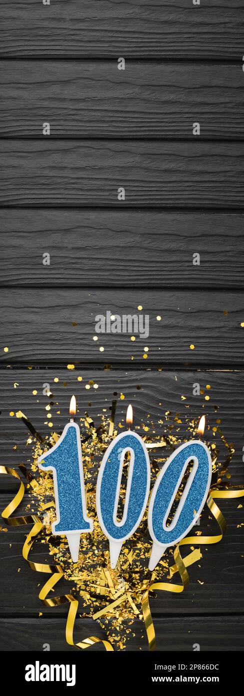 Number 100 blue celebration candle and gold confetti on dark wooden ...