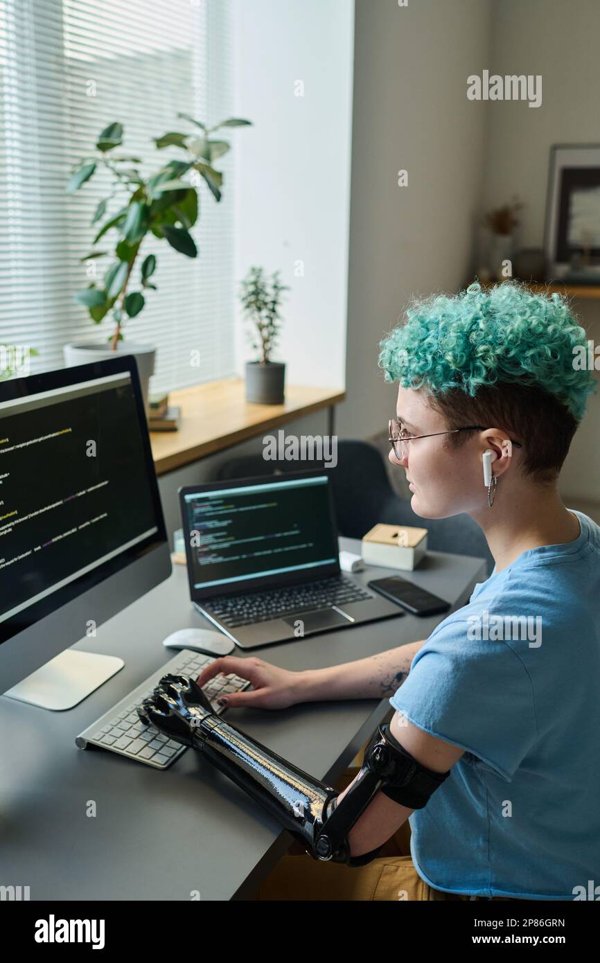 Vertical image of young programmer with prosthetic arm working with computer codes on computer ...