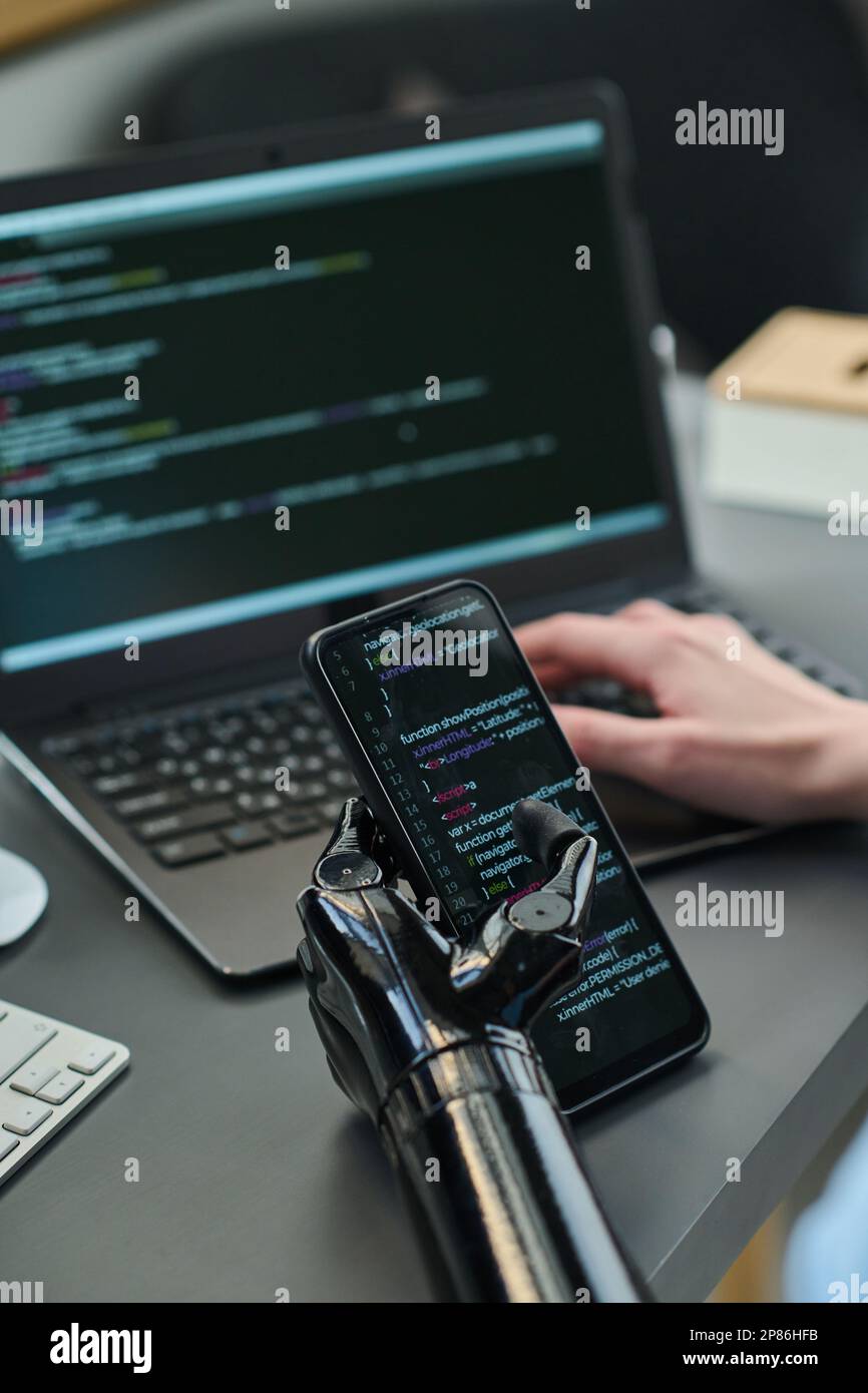 Vertical image of programmer with prosthetic arm connecting smartphone with laptop and typing ...