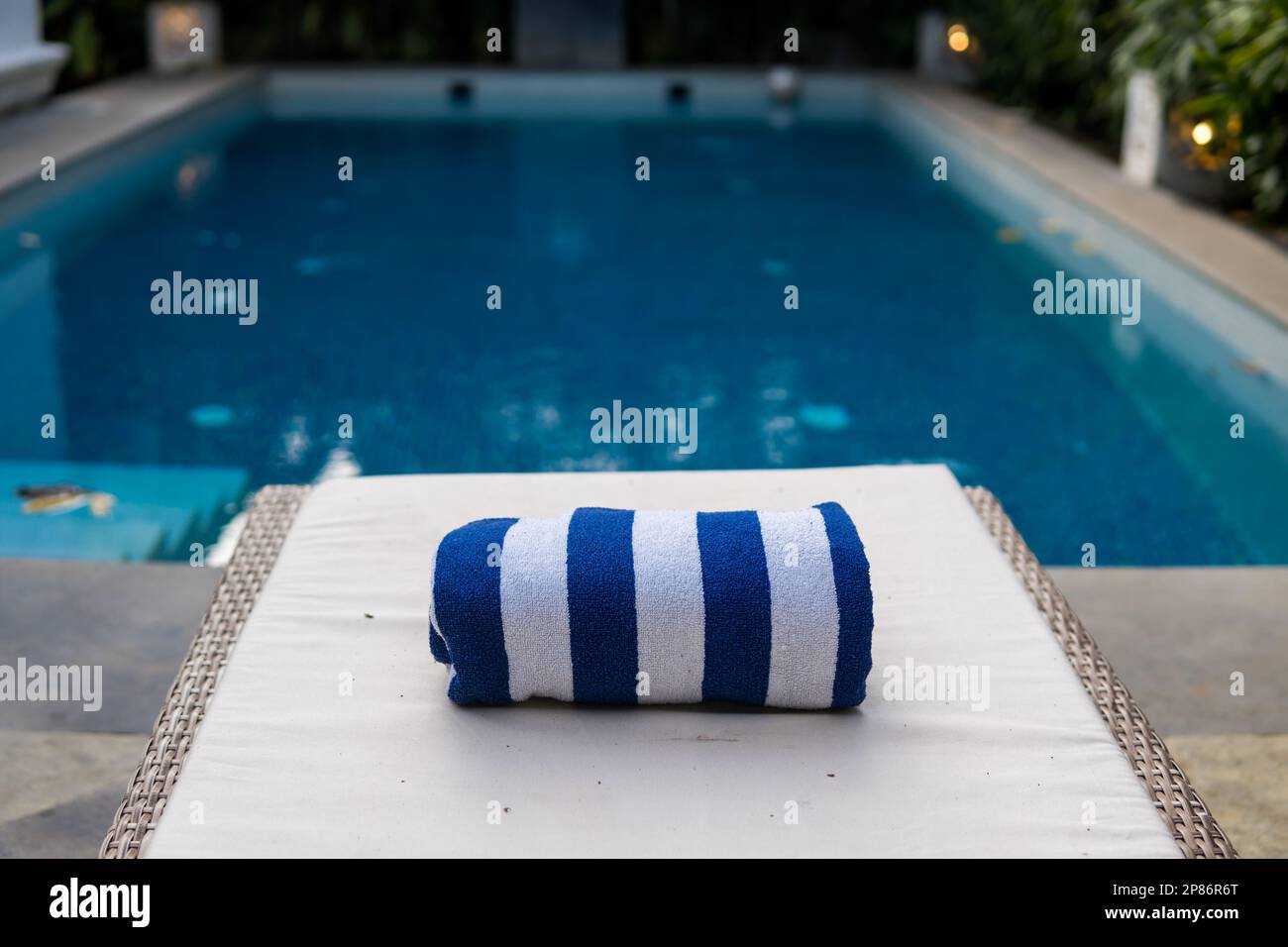 Blue striped bath towel on a chaise lounge near a private swimming pool ...