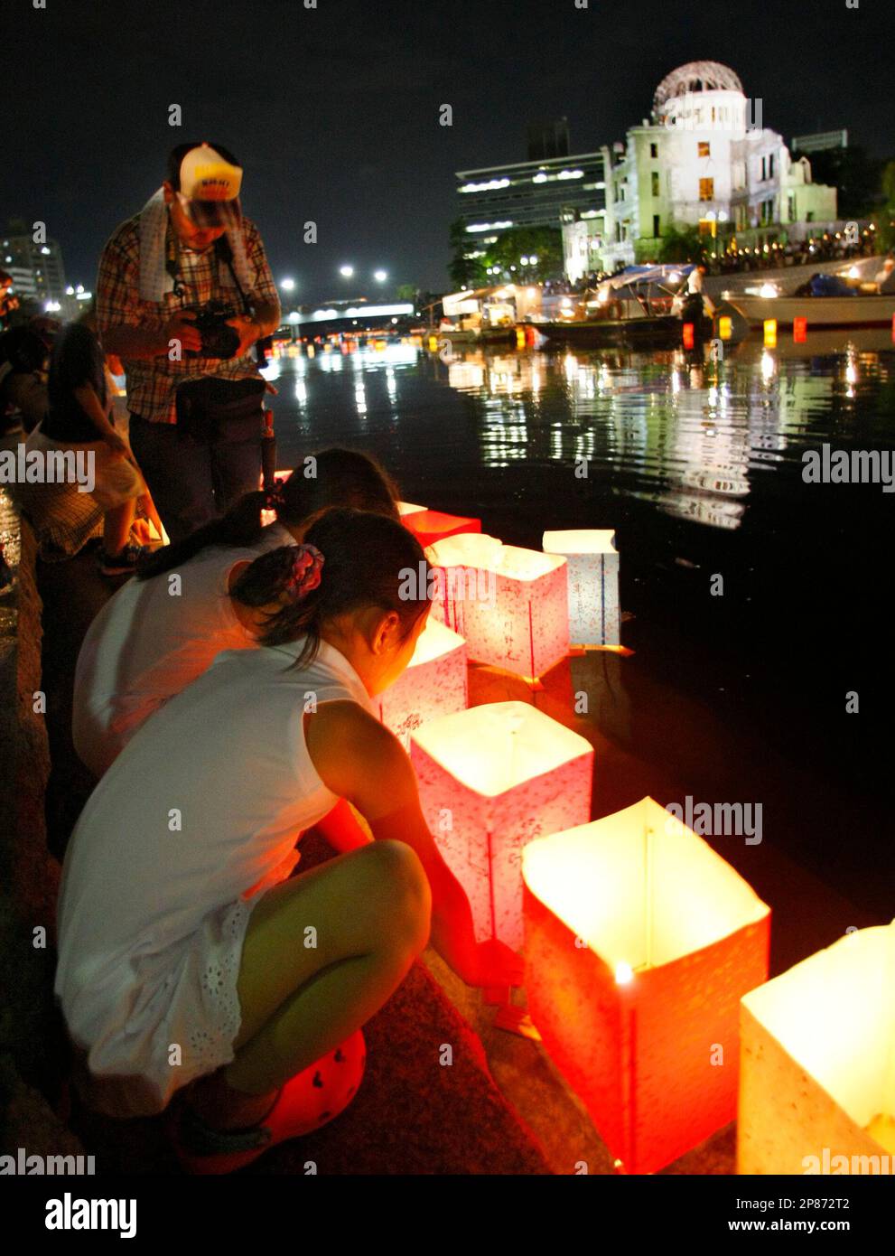 A girl releases a paper lantern in the Motoyasu River with the backdrop ...
