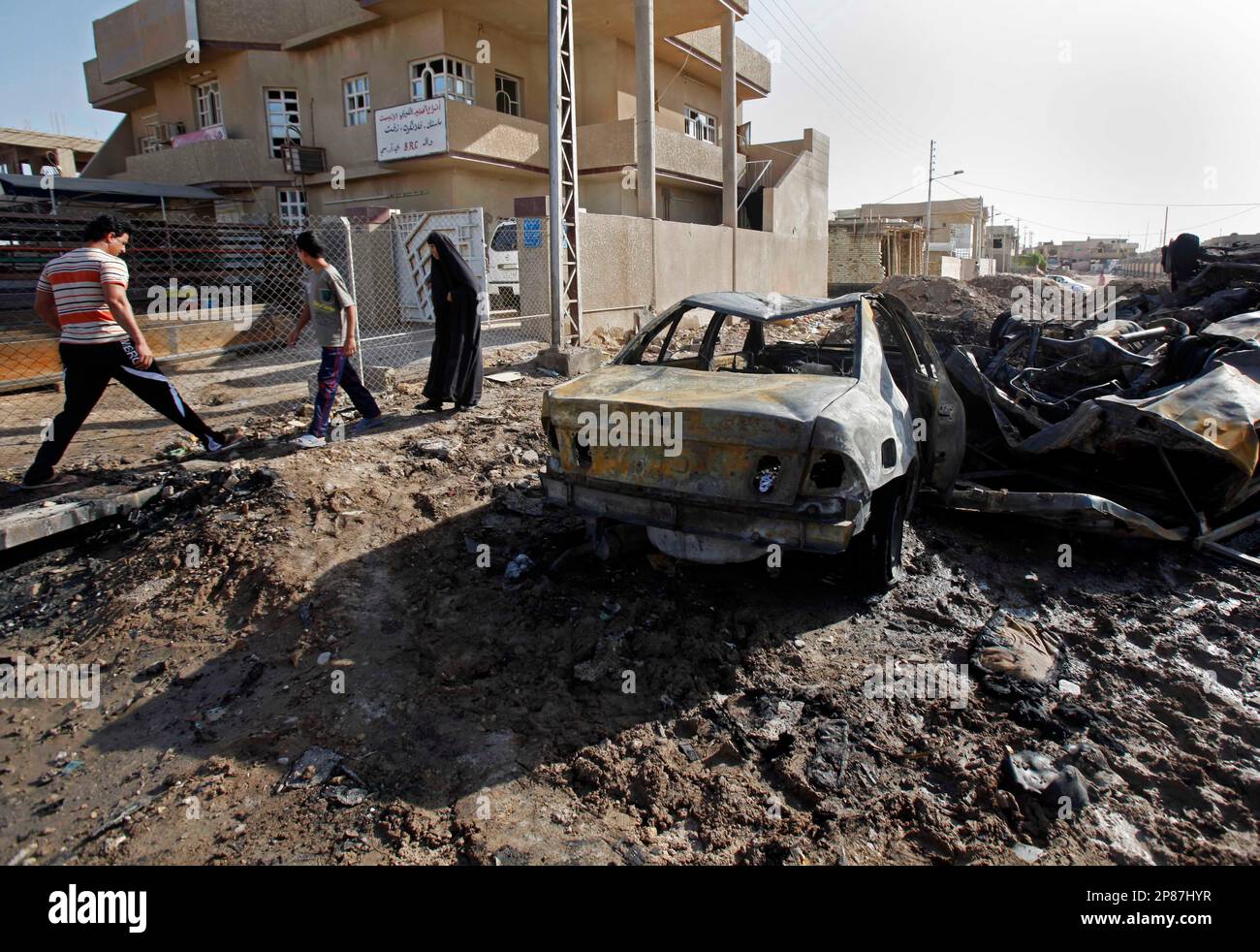 Iraqis walk past cars destroyed in a car bomb explosion in a parking ...