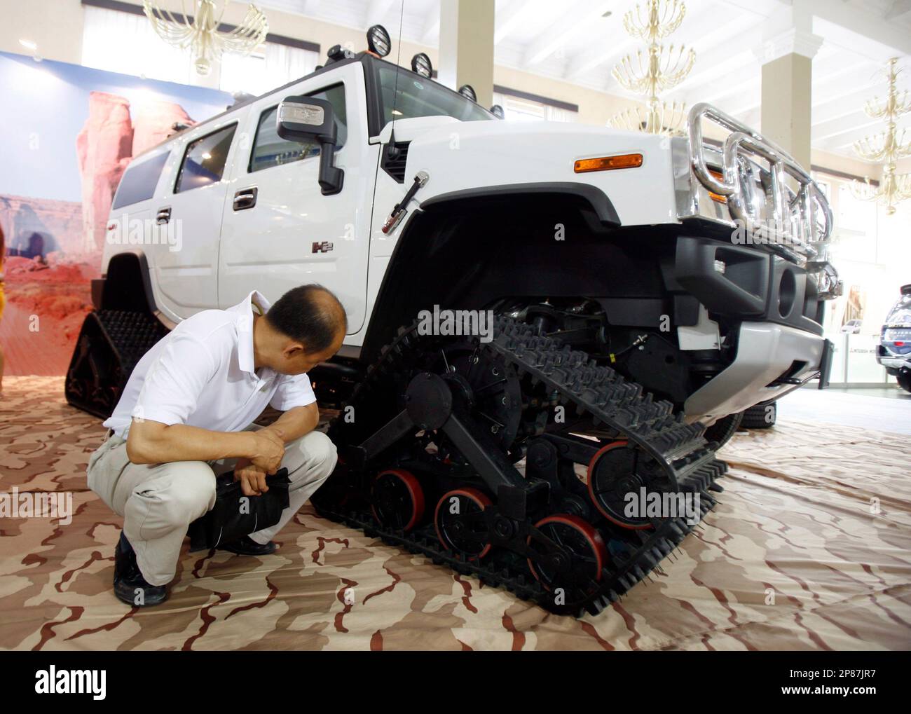 A man looks at a Hummer with tracks in place of wheels at an auto ...