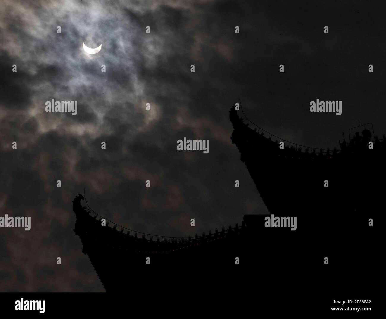 A partial solar eclipse is seen through clouds over Chinese traditional ...