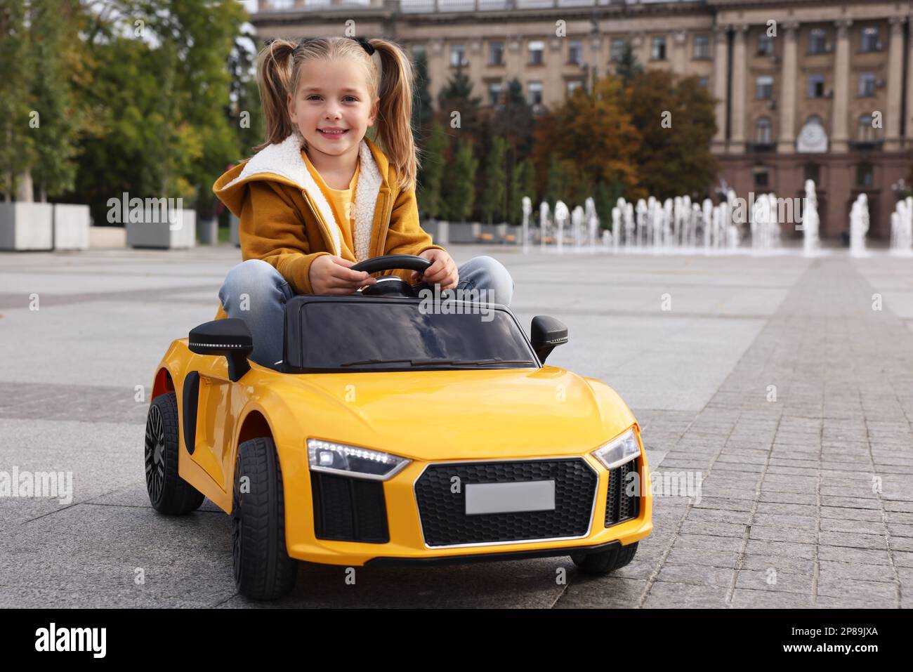 Cute little girl driving children's car on city street Stock Photo - Alamy