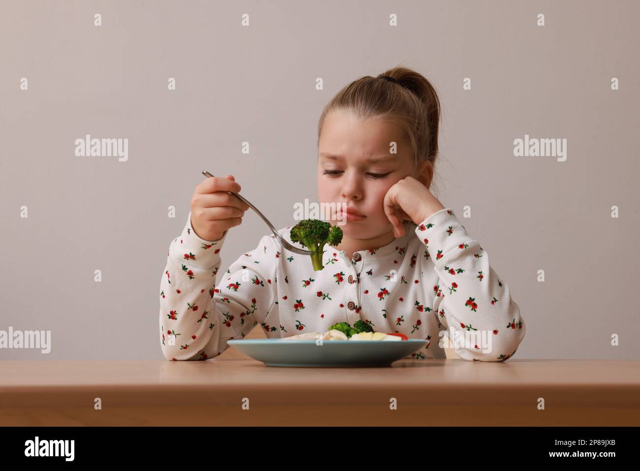 Cute little girl refusing to eat her dinner at table on grey background ...