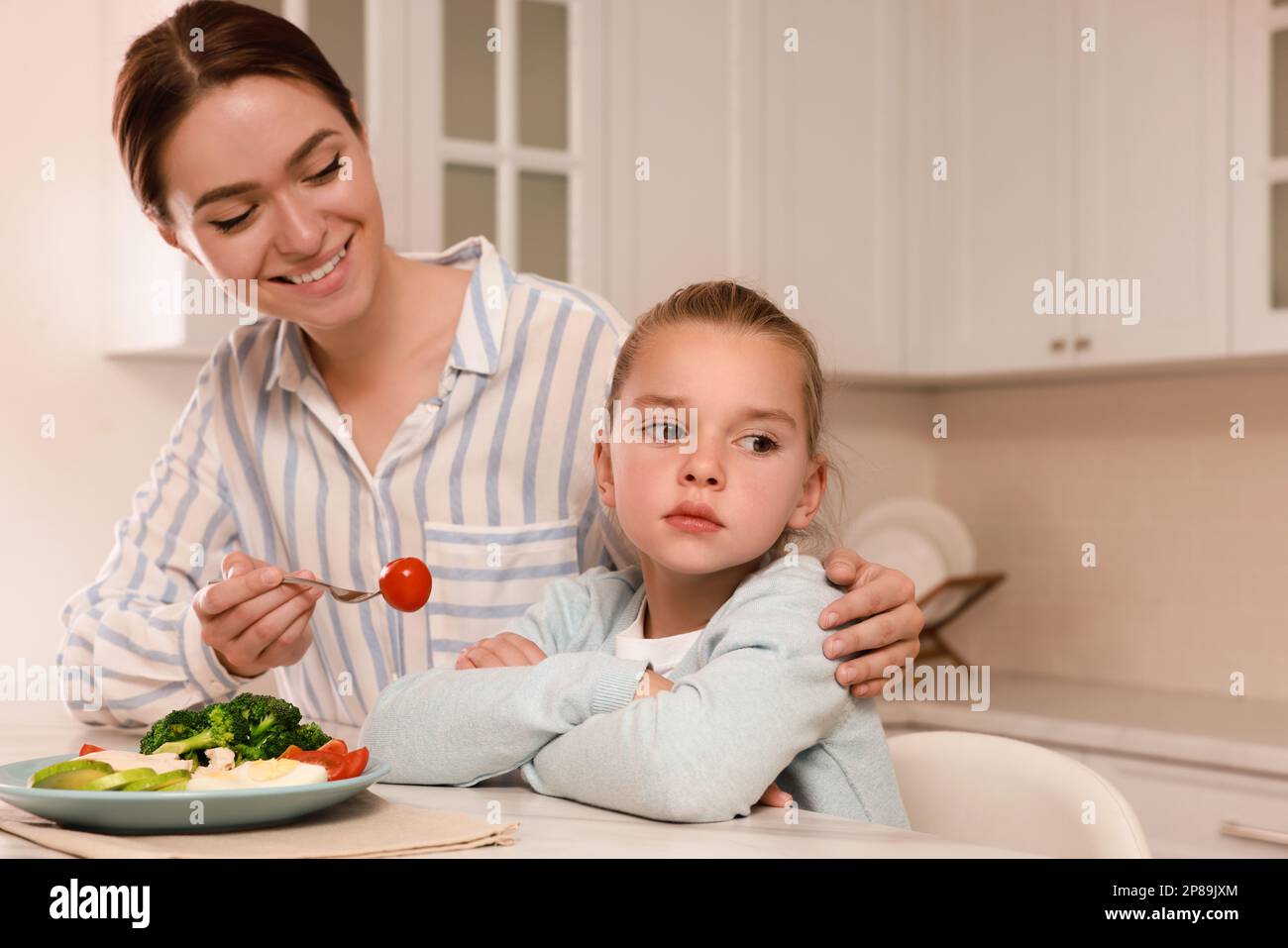 Mother feeding her daughter in kitchen. Little girl refusing to eat ...