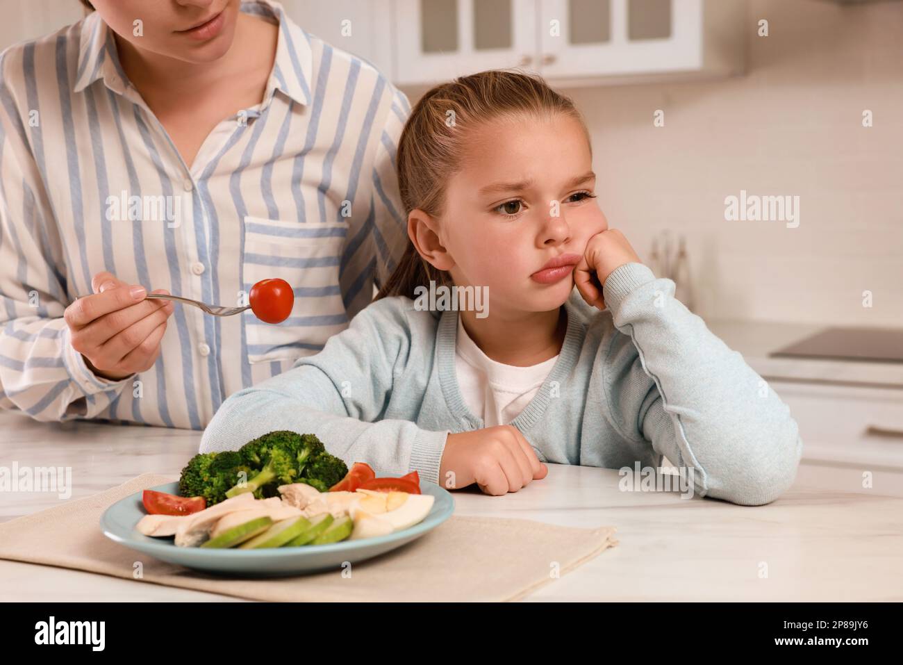 Mother feeding her daughter in kitchen, closeup. Little girl refusing ...
