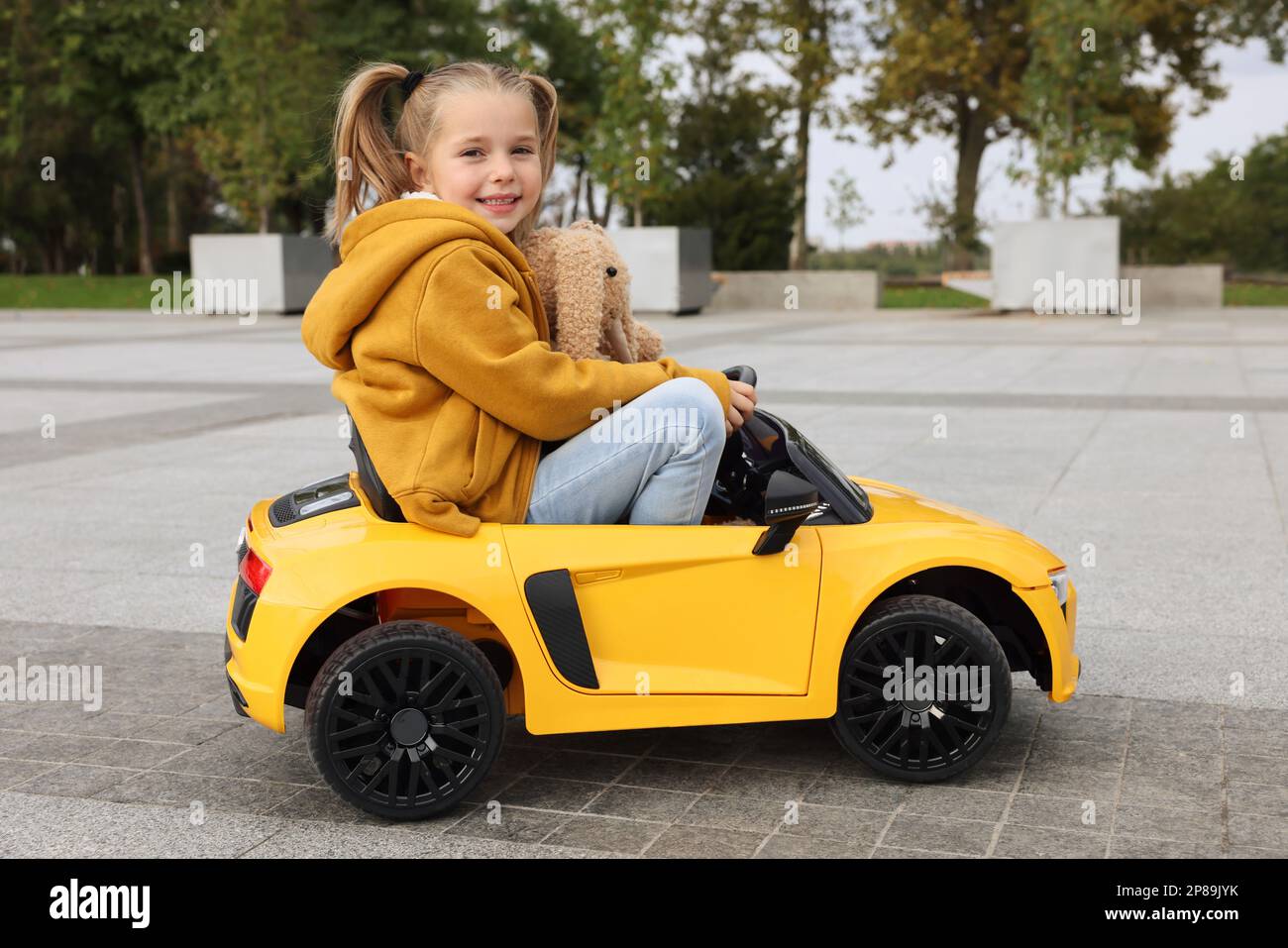 Cute little girl with toy bunny driving children's car on city street ...