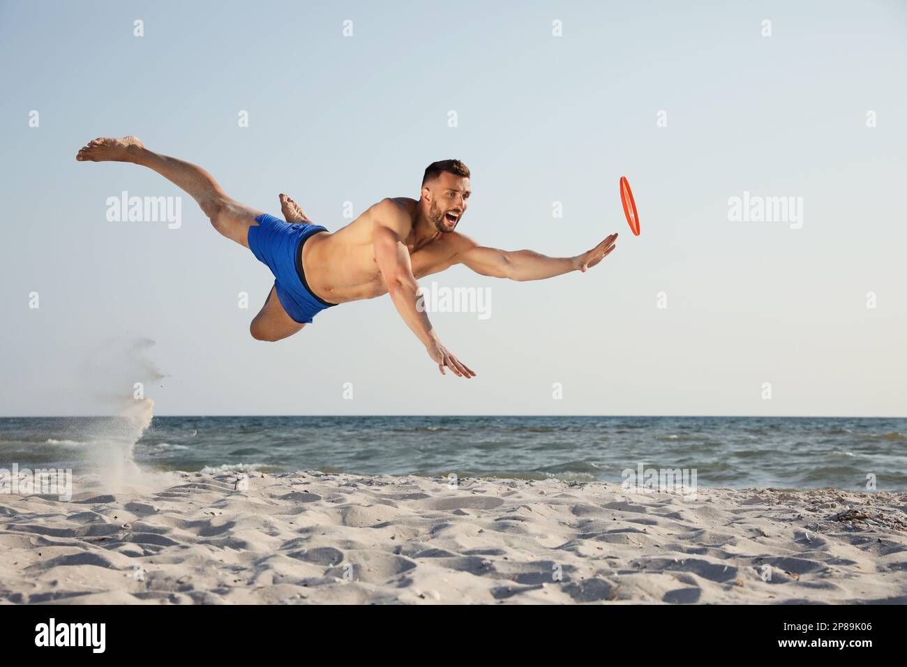 Sportive man jumping while trying to catch flying disk at beach Stock ...