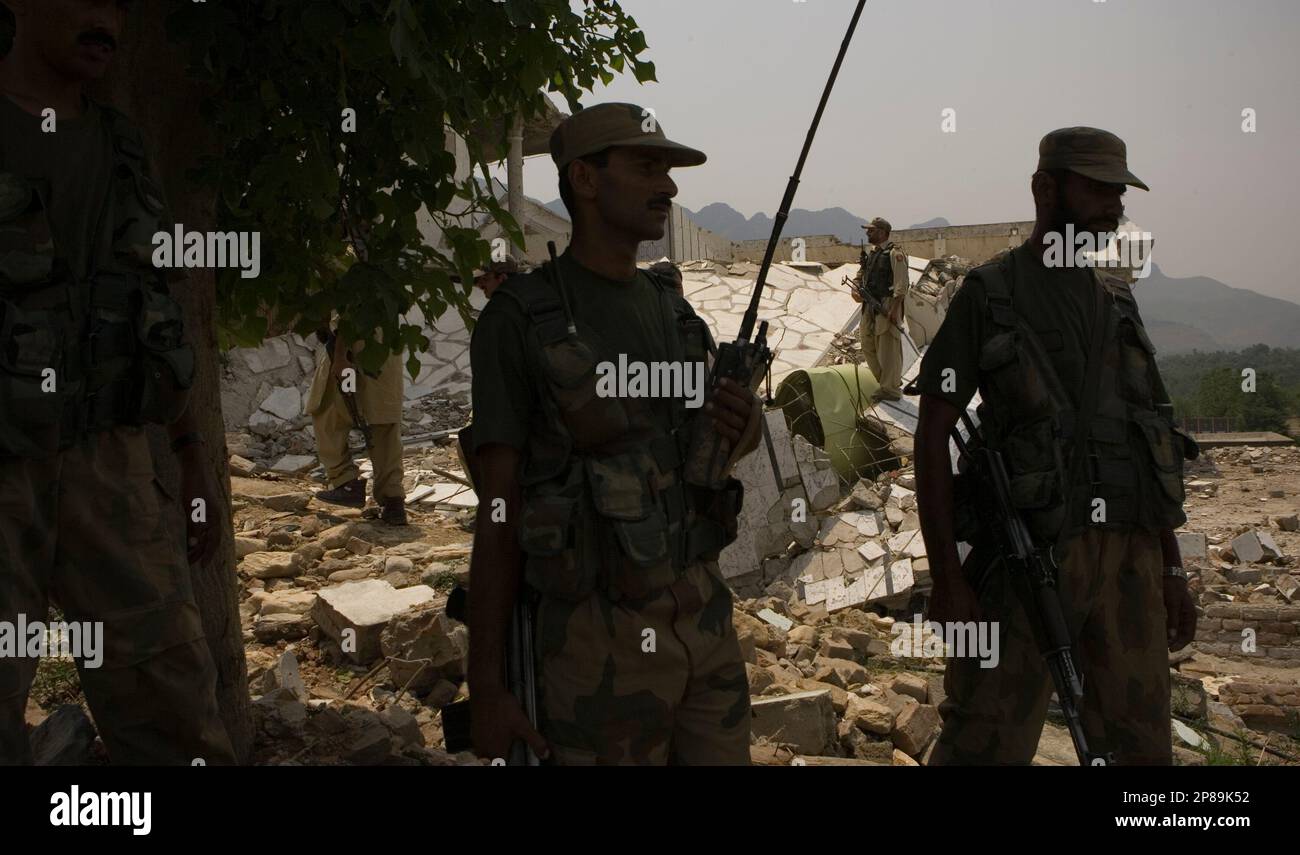 Pakistani security forces officers stand over debris of houses in ...