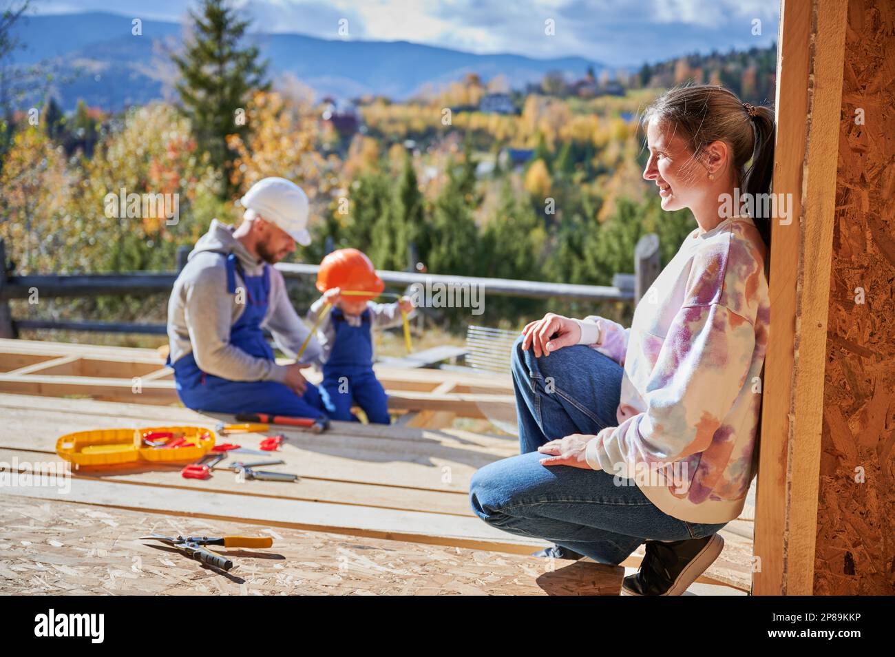 Father, mother and son building wooden frame house. Toddler boy helping ...