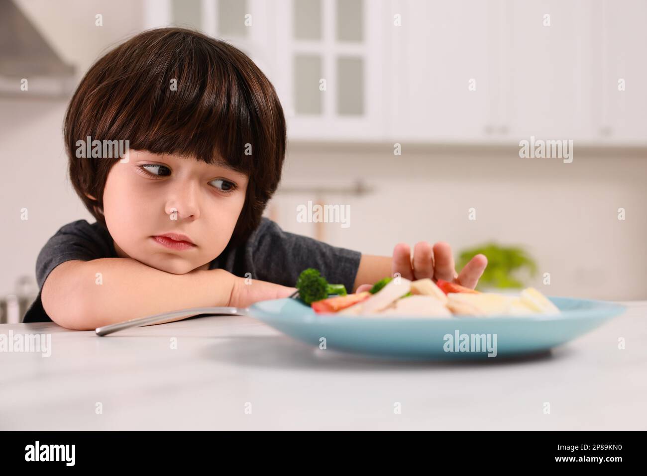 Cute little boy refusing to eat dinner in kitchen Stock Photo - Alamy