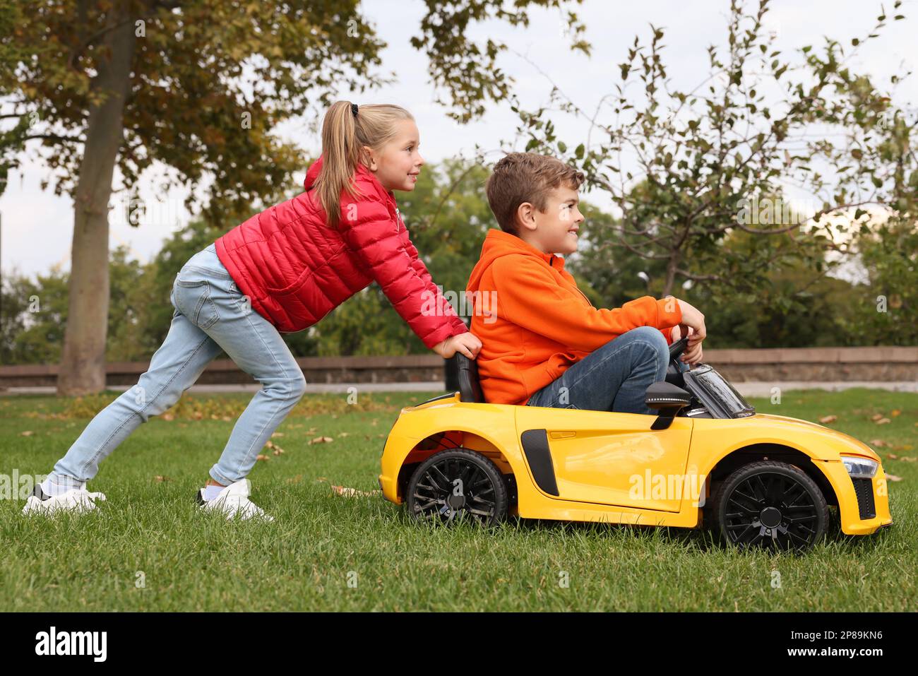 Cute girl pushing children's car with little boy in park Stock Photo ...