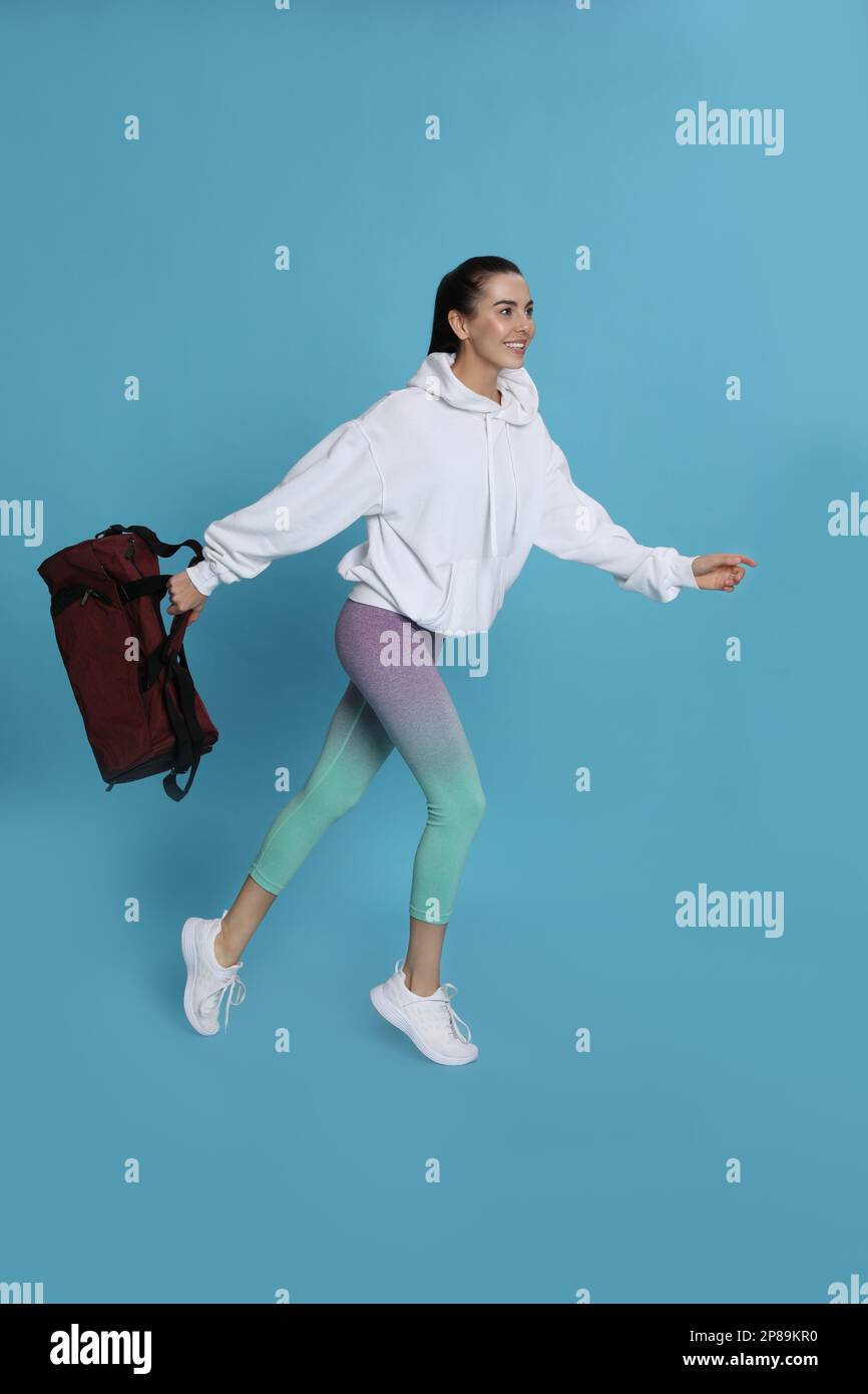 Beautiful woman with sports bag running on light blue background Stock ...