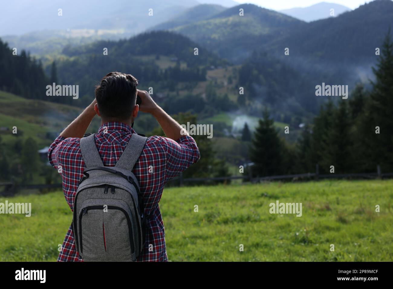 Tourist with backpack and binoculars enjoying landscape in mountains ...