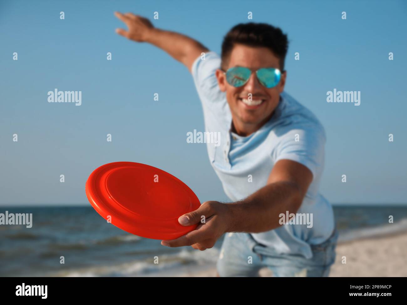 Happy man throwing flying disk at beach, focus on hand Stock Photo - Alamy
