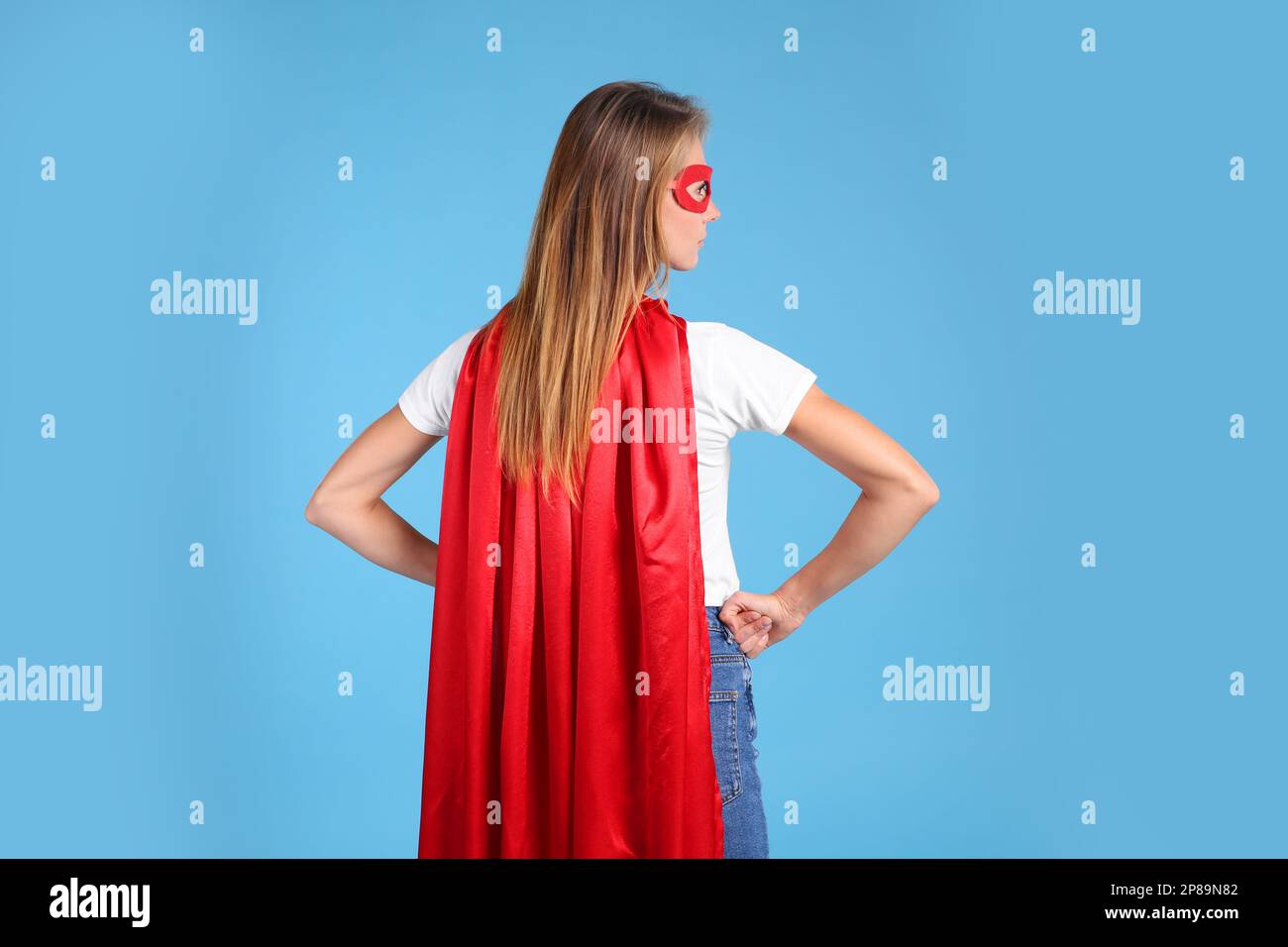 Woman wearing superhero cape and mask on light blue background, back ...