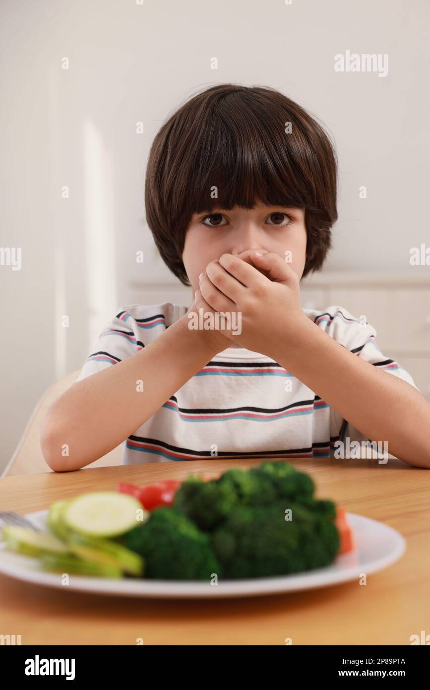 Cute little boy covering mouth and refusing to eat vegetables at home ...