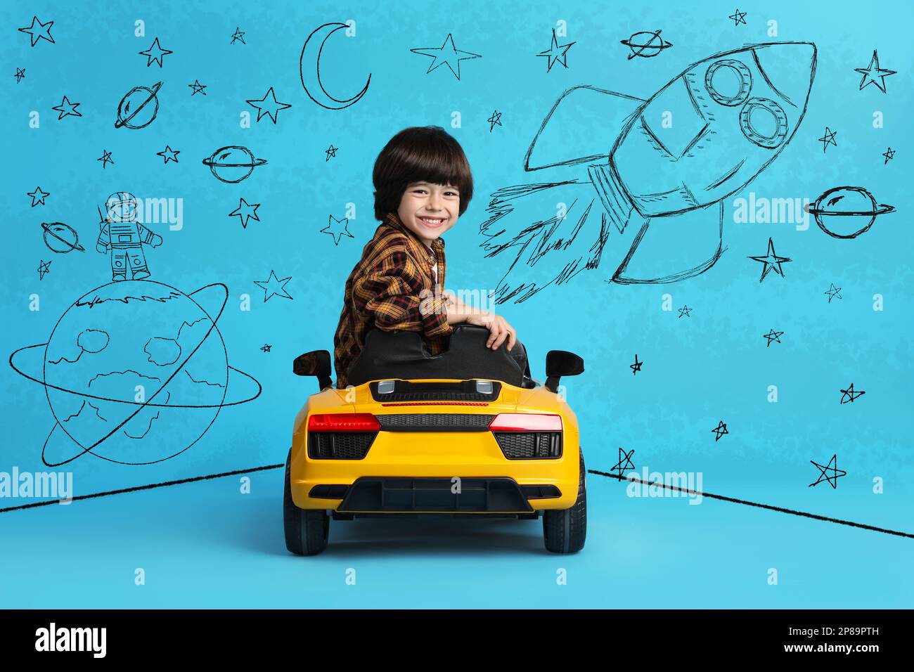 Cute little boy driving toy car and drawing of space on light blue ...