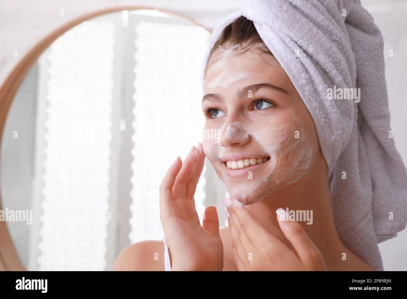 Beautiful teenage girl applying cleansing foam onto face in bathroom ...