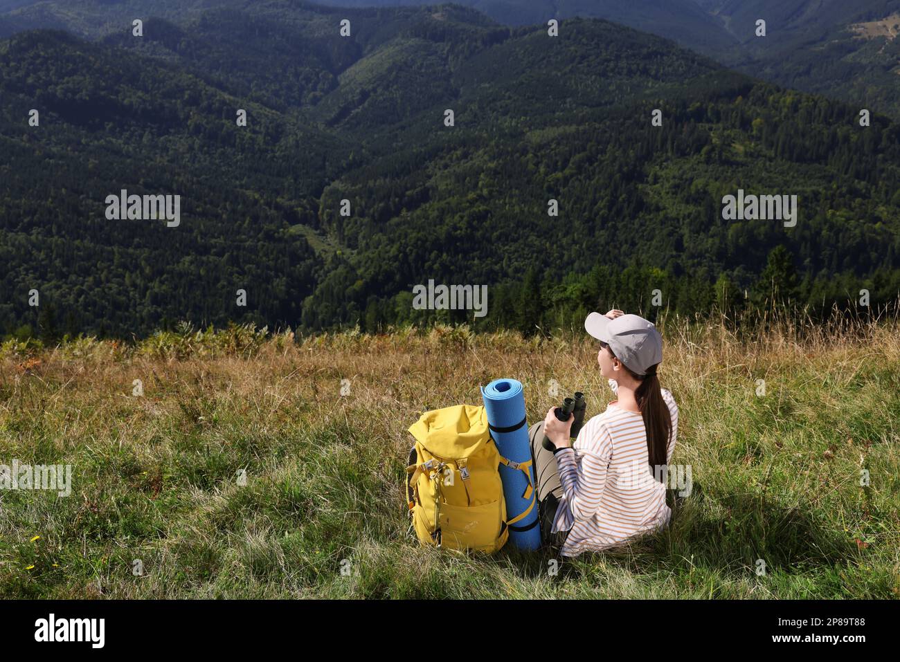Tourist with hiking equipment looking through binoculars in mountains ...