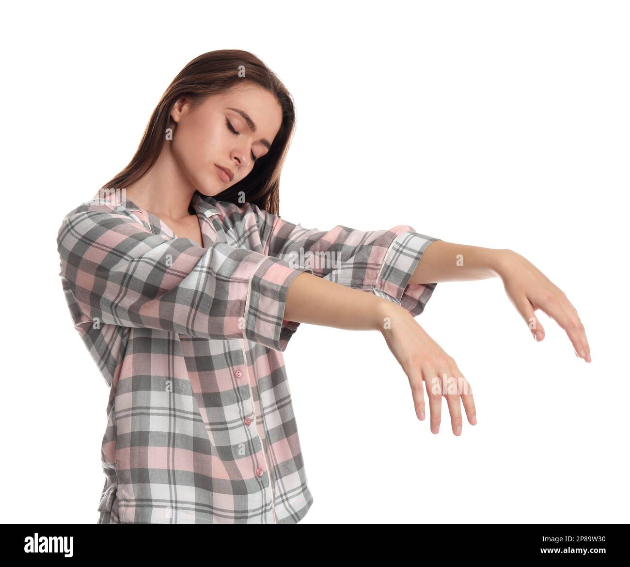 Young woman wearing pajamas in sleepwalking state on white background ...