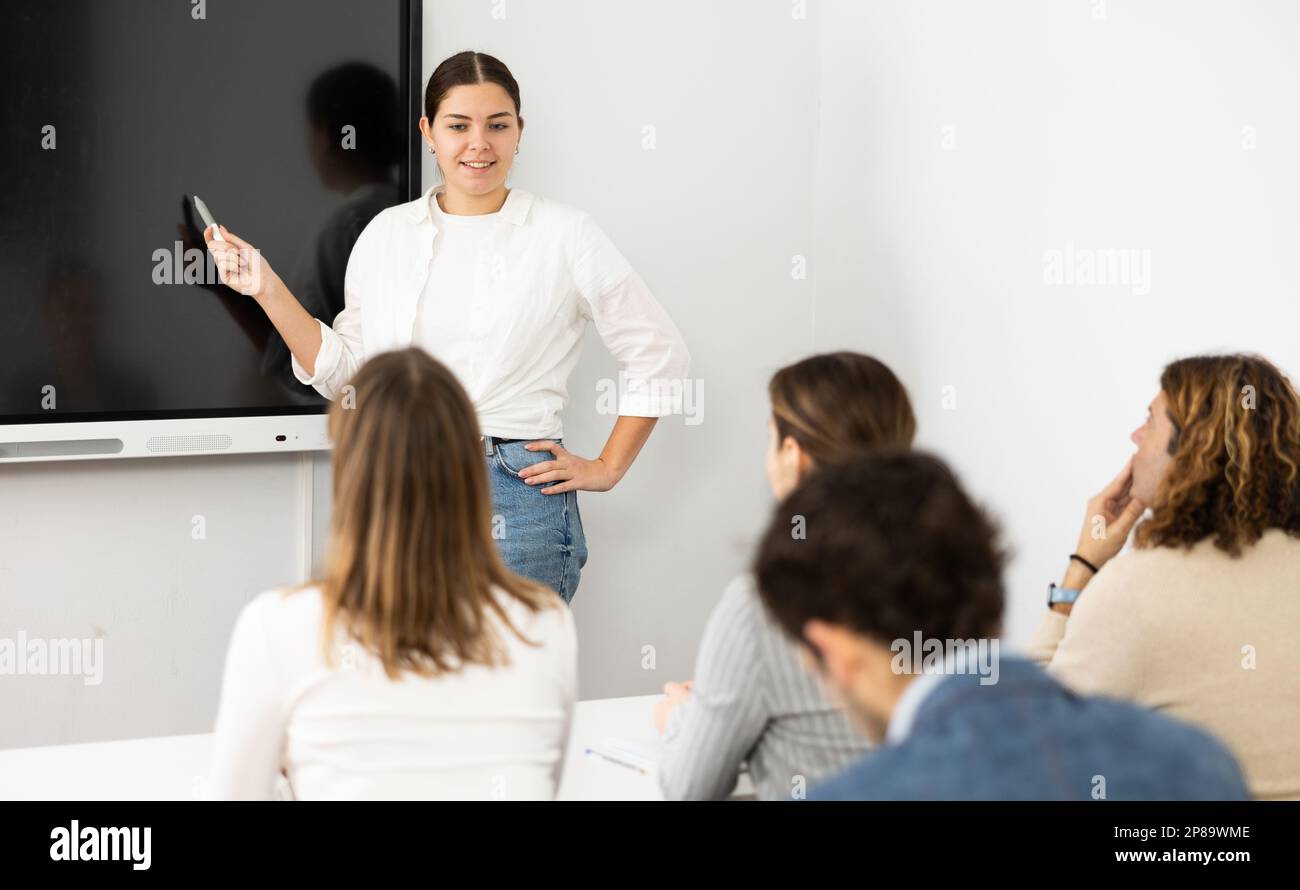 Young female professor explaining subject to classroom full of students ...