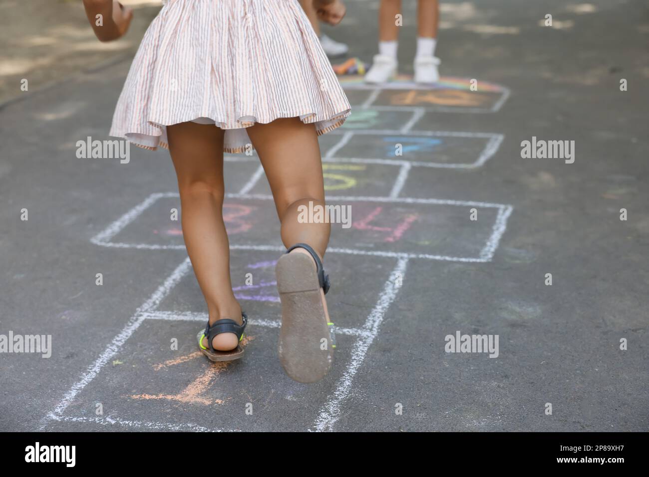 Little children playing hopscotch drawn with chalk on asphalt outdoors ...