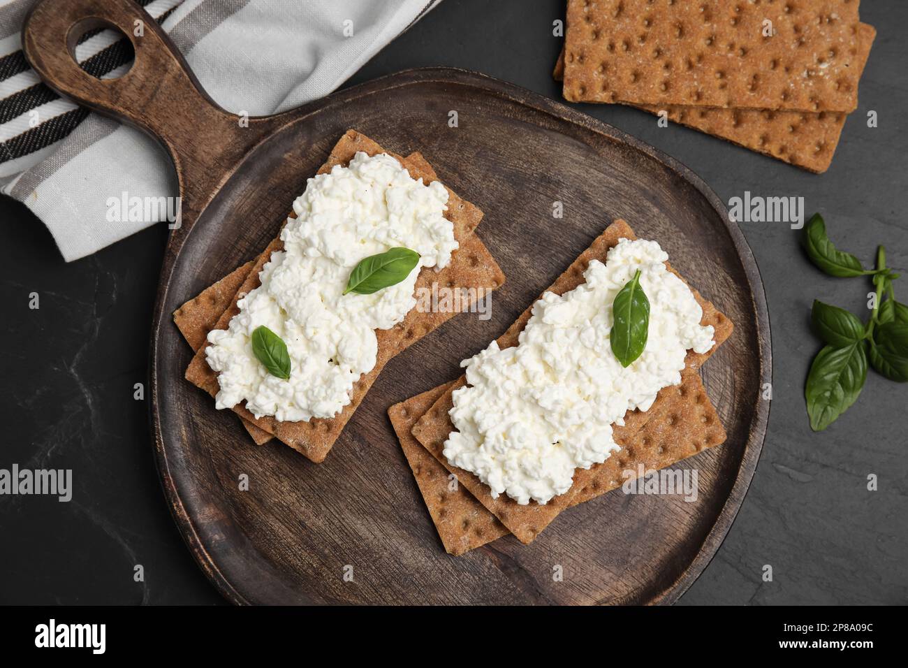 Crispy crackers with cottage cheese and basil on black table, flat lay ...
