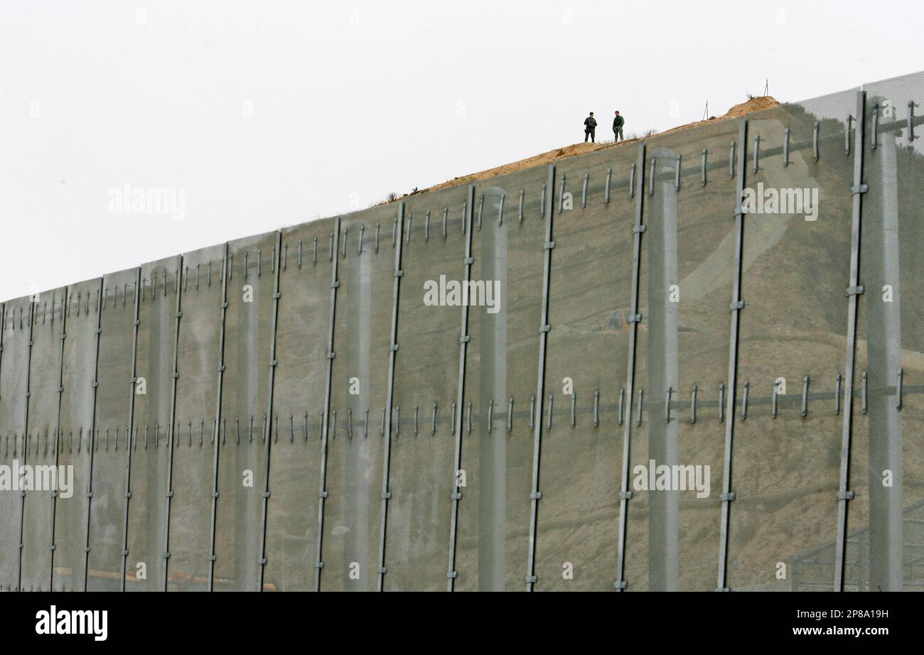 Two U.S. Border Patrol agents stand on the U.S. side of a section of ...