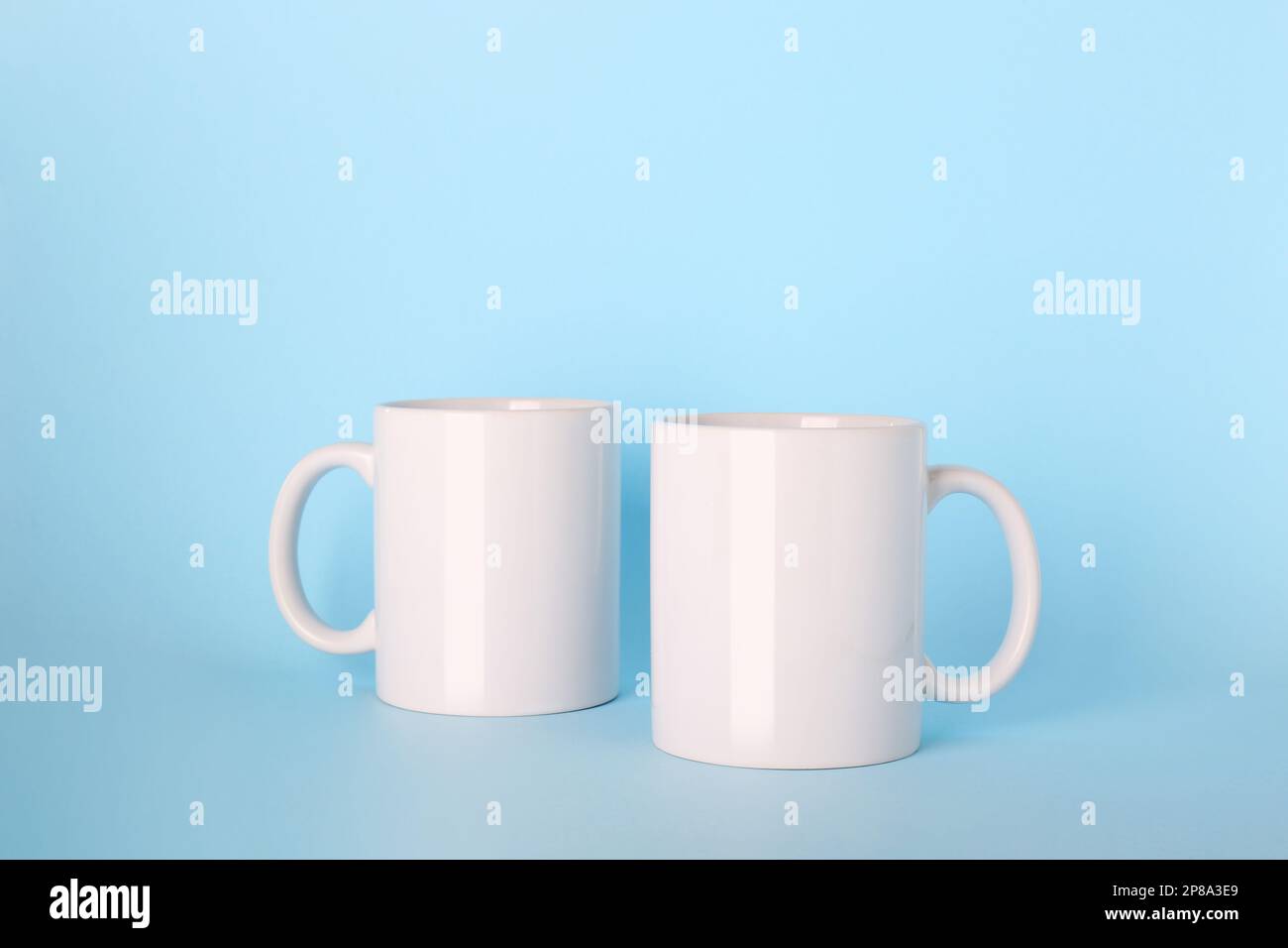 Blank white ceramic mugs on light blue background Stock Photo - Alamy