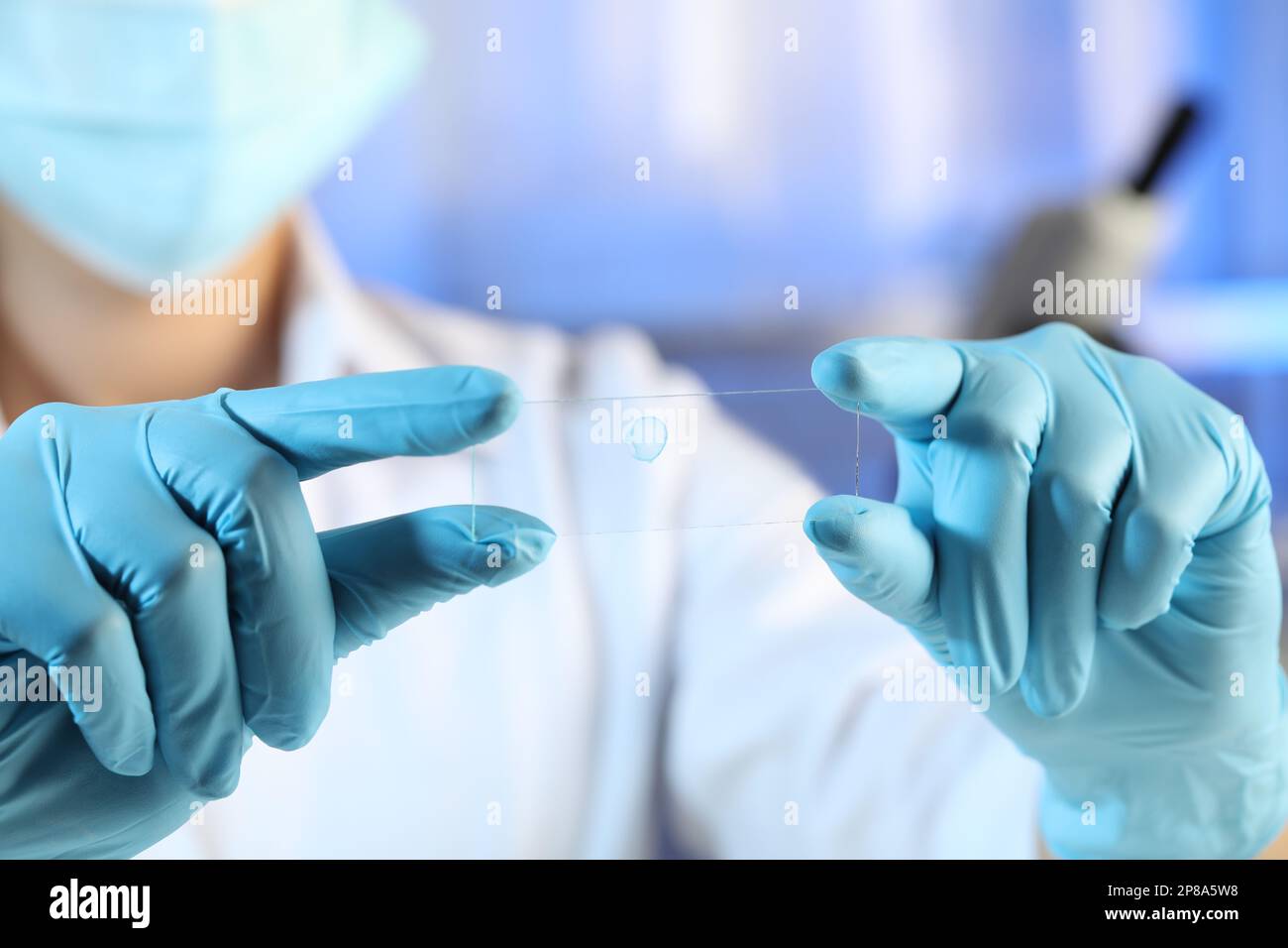 Scientist holding microscope slide with light blue sample in laboratory ...