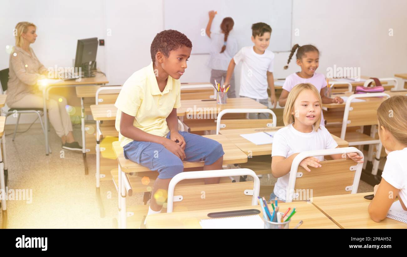 Positive primary school students are talking about homework at desk ...