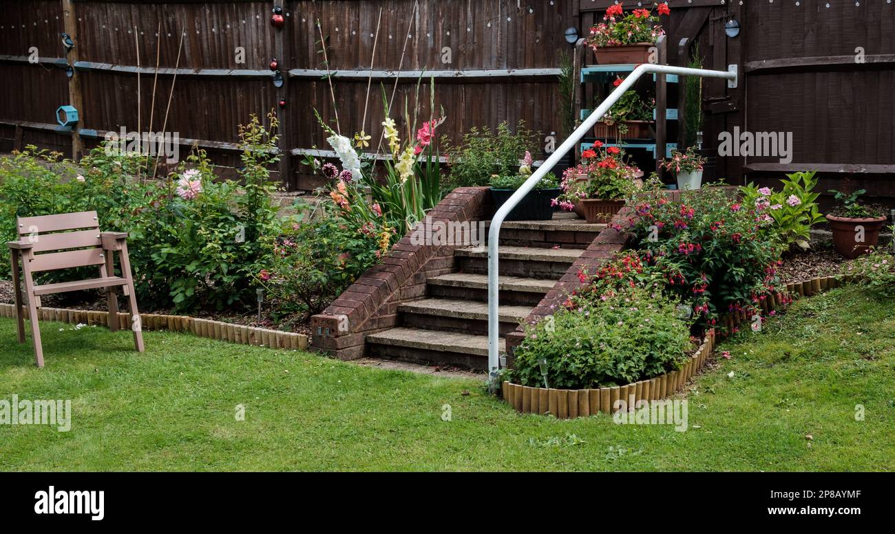 A garden with assorted flowers & shrubs bordering a lawn, wooden chair ...