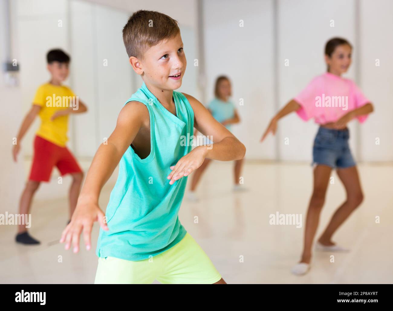 Cheerful preteen boy learning energetic dance moves in choreography ...