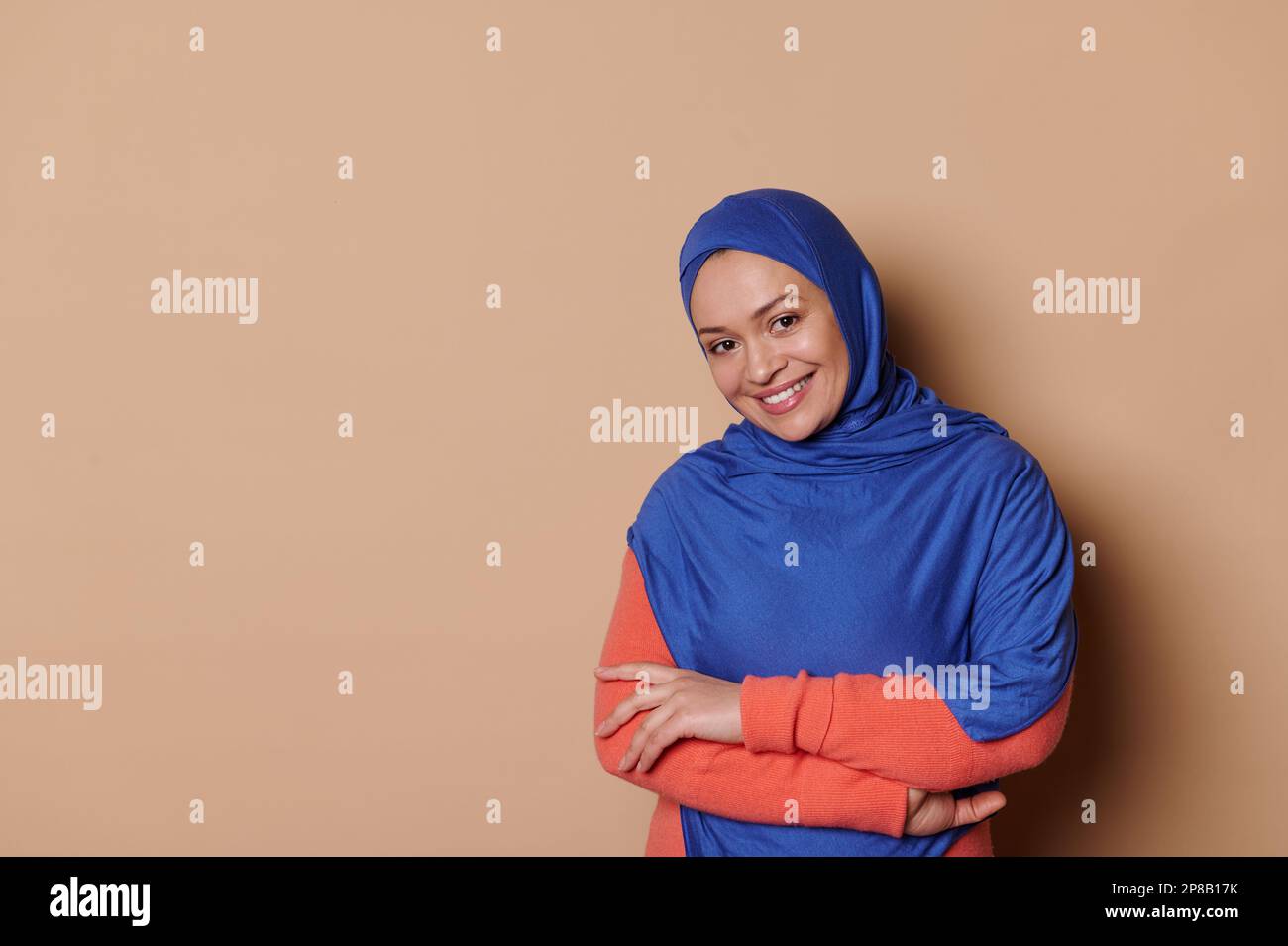 Arab Muslim woman in blue hijab, smiling looking at camera, beige ...