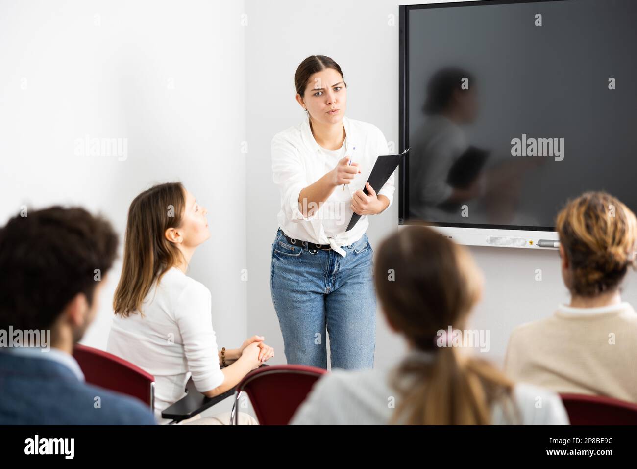Young female professor explaining subject to classroom full of students ...