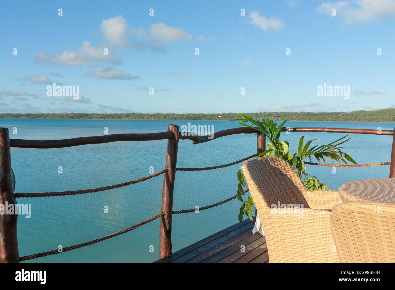 Rustic railing around deck over water with furniture and pot plant on ...
