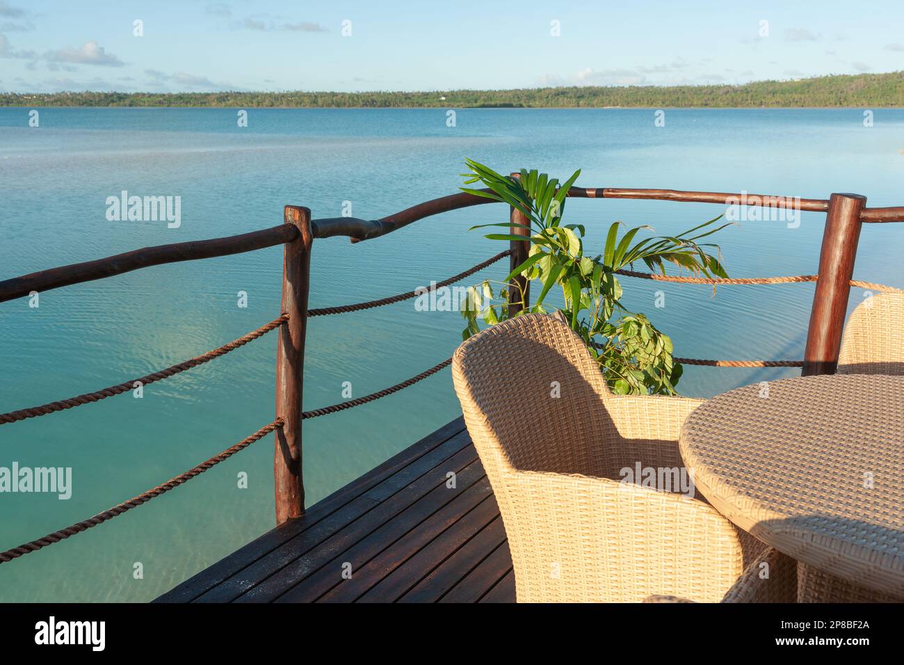 Rustic railing around deck over water with furniture and pot plant on ...