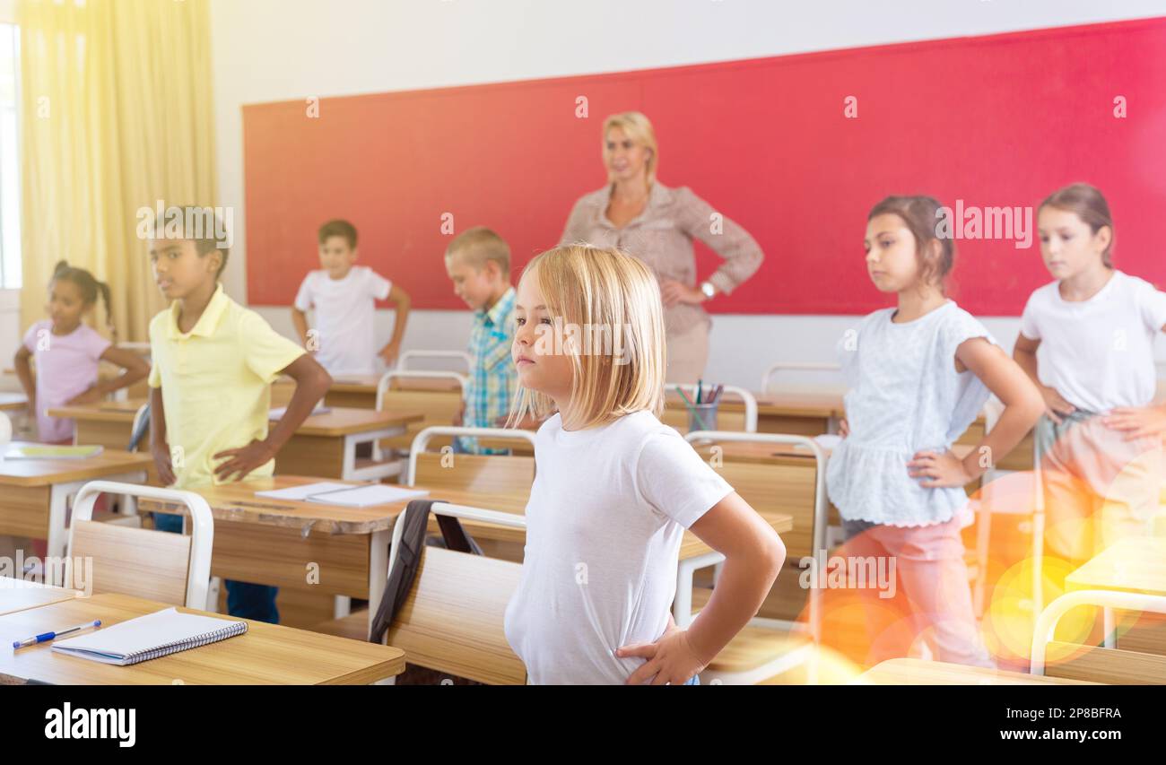 Preteen schoolchildren with teacher performing physical exercises in ...