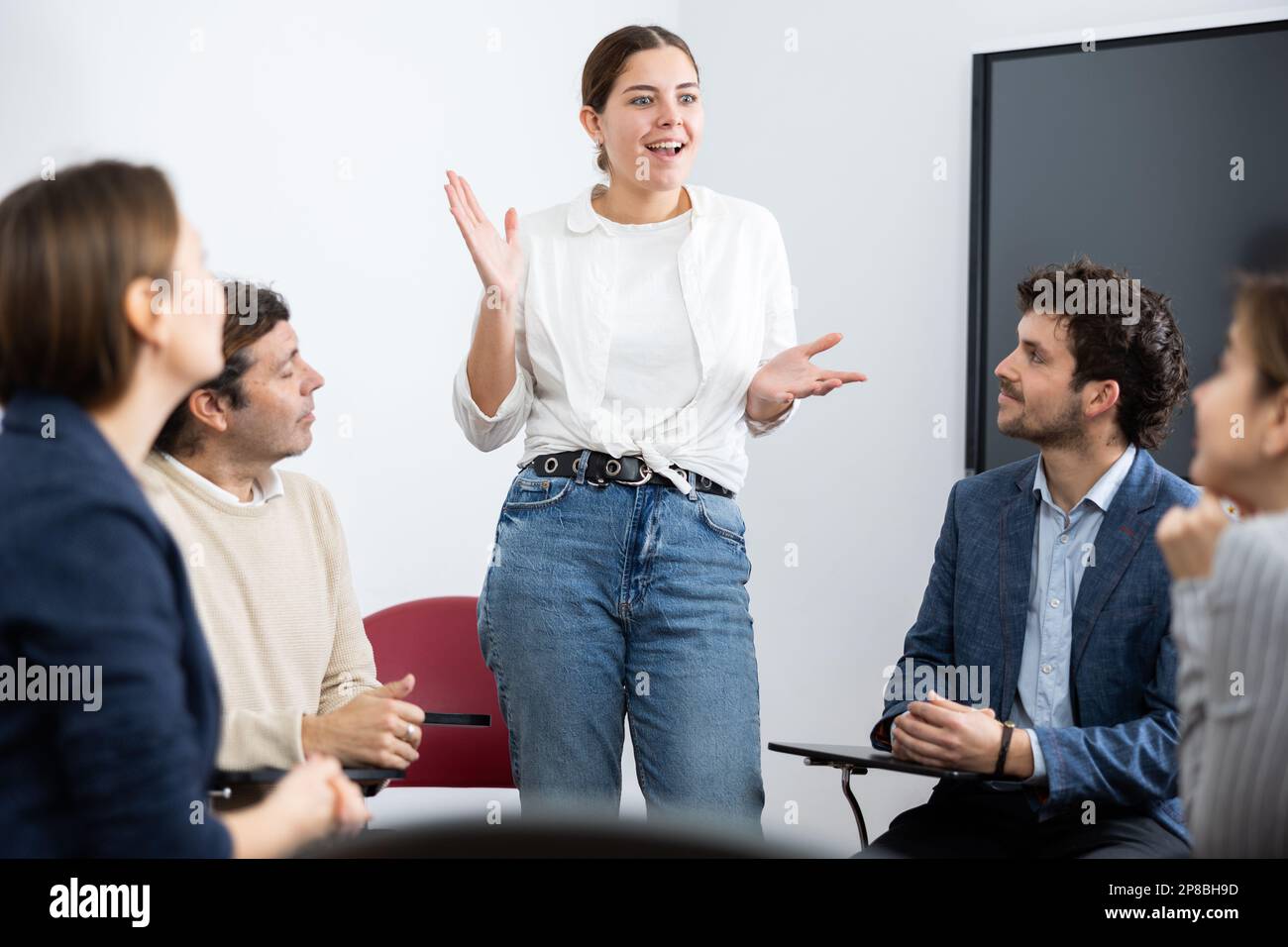 Young female professor explaining subject to classroom full of students ...