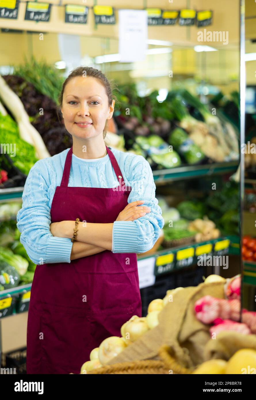 Joyful skilled adult female seller in uniform posing during working day ...