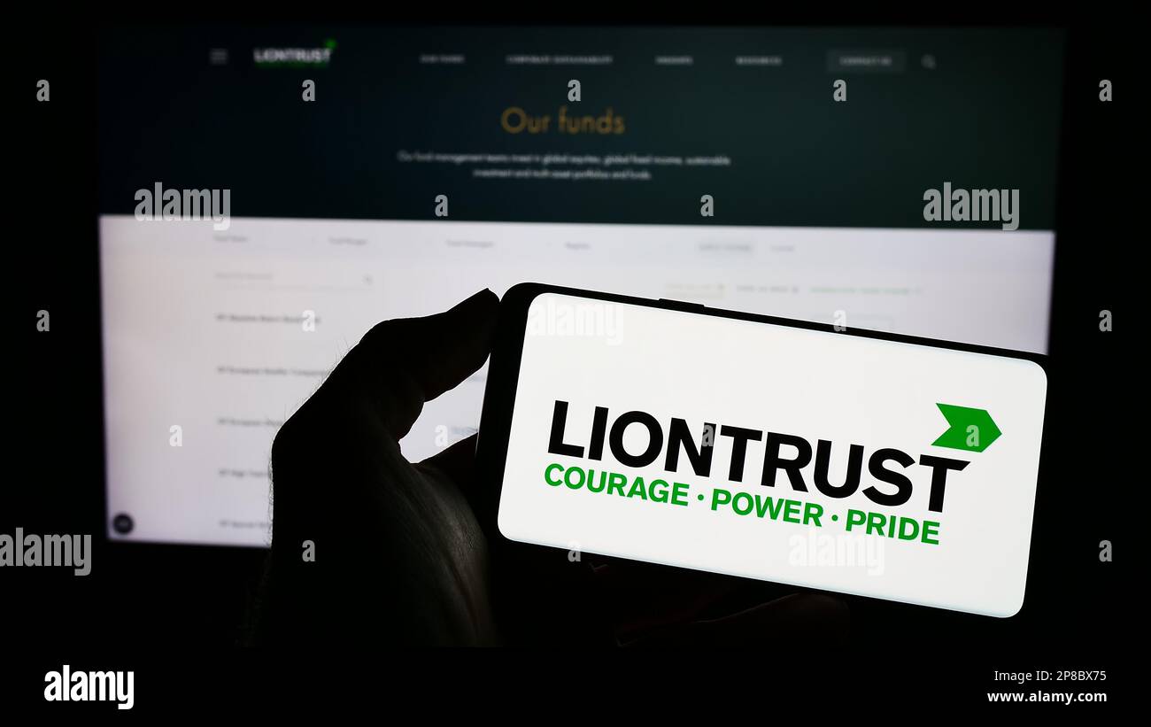 Person holding cellphone with logo of British company Liontrust Asset Management plc on screen ...