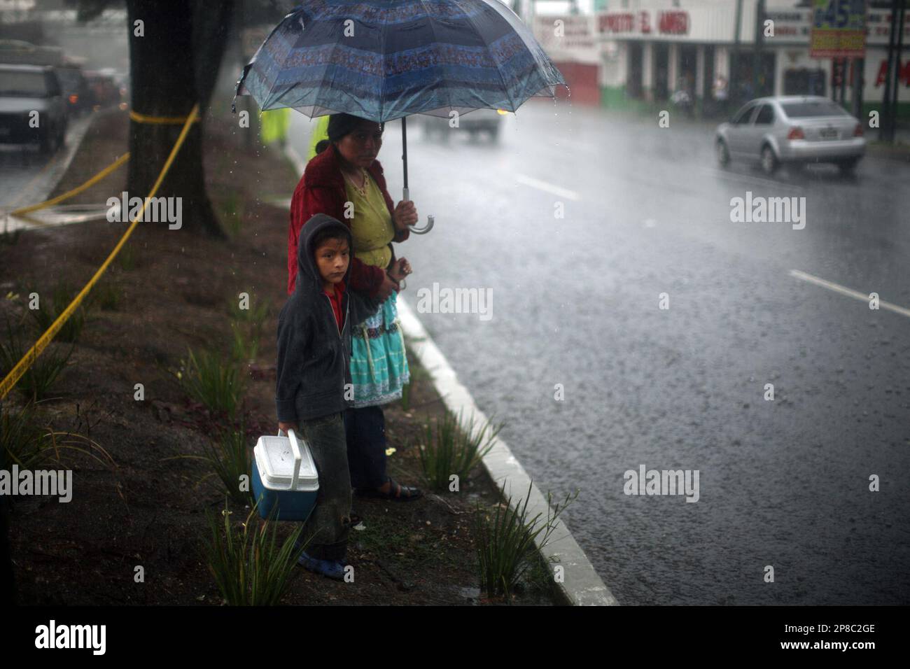 A woman tries to cross an avenue with a child under heavy rain in ...