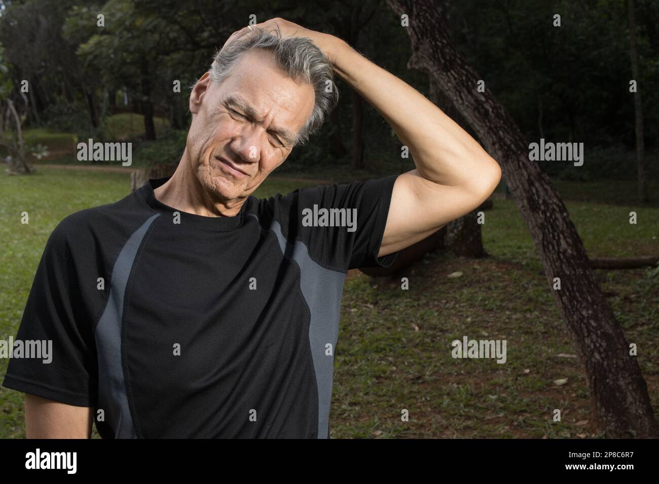 Mature Man outside at a park sitting on a tree stump stretching out his ...