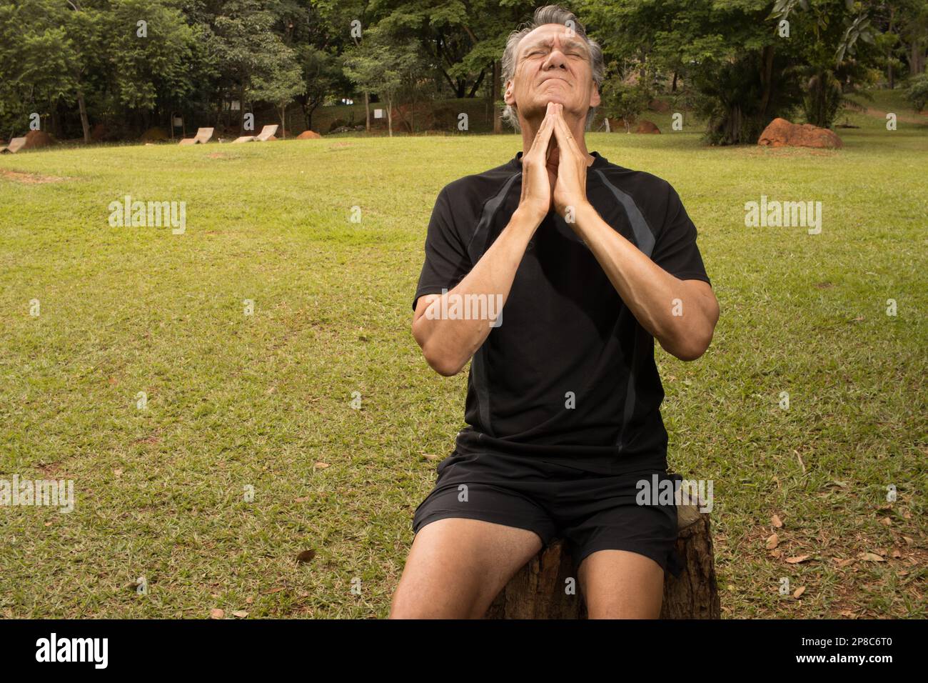 Mature Man outside at a park sitting on a tree stump stretching out his ...